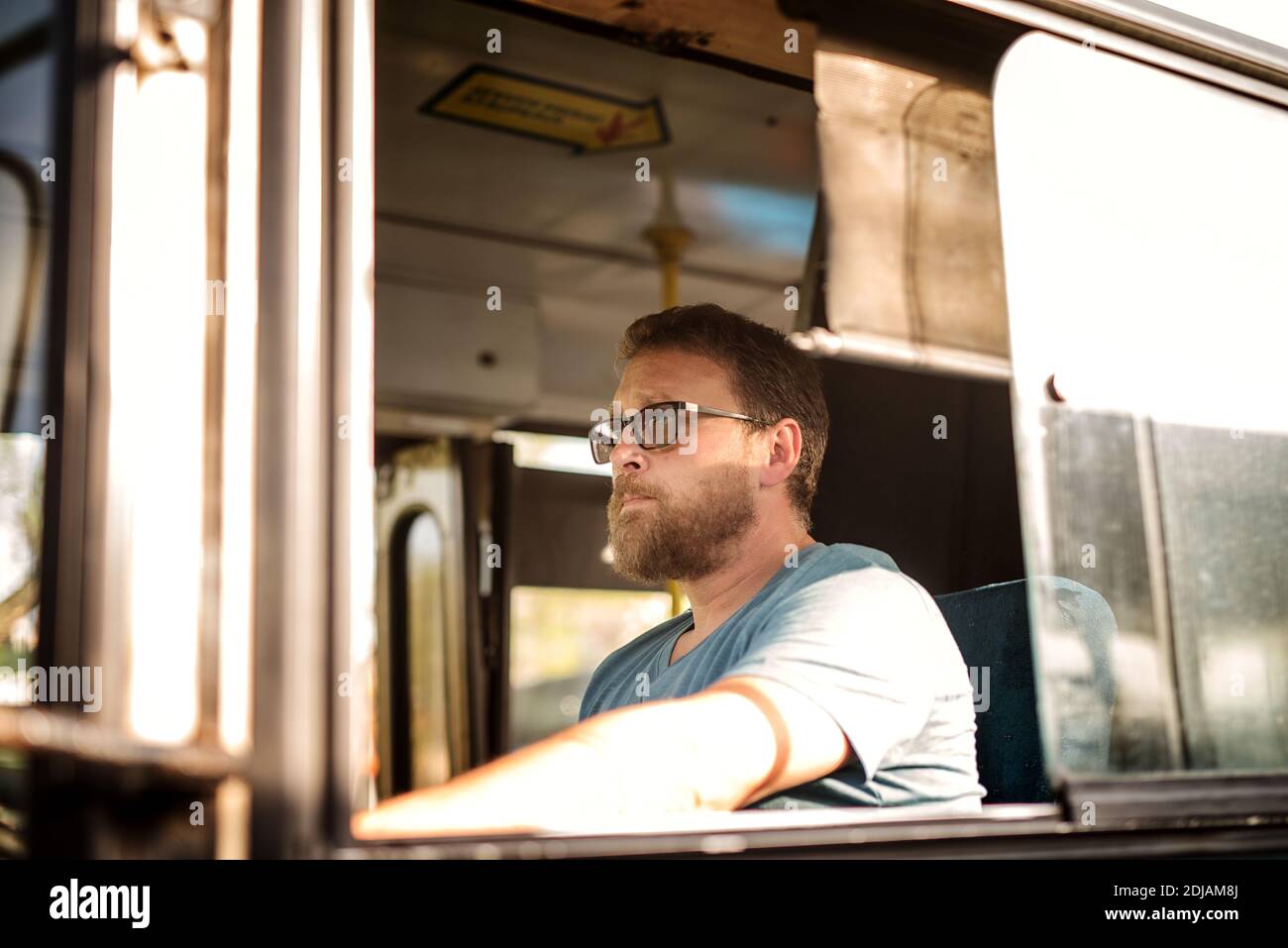Focused young bus driver is patiently waiting for passengers to board ...