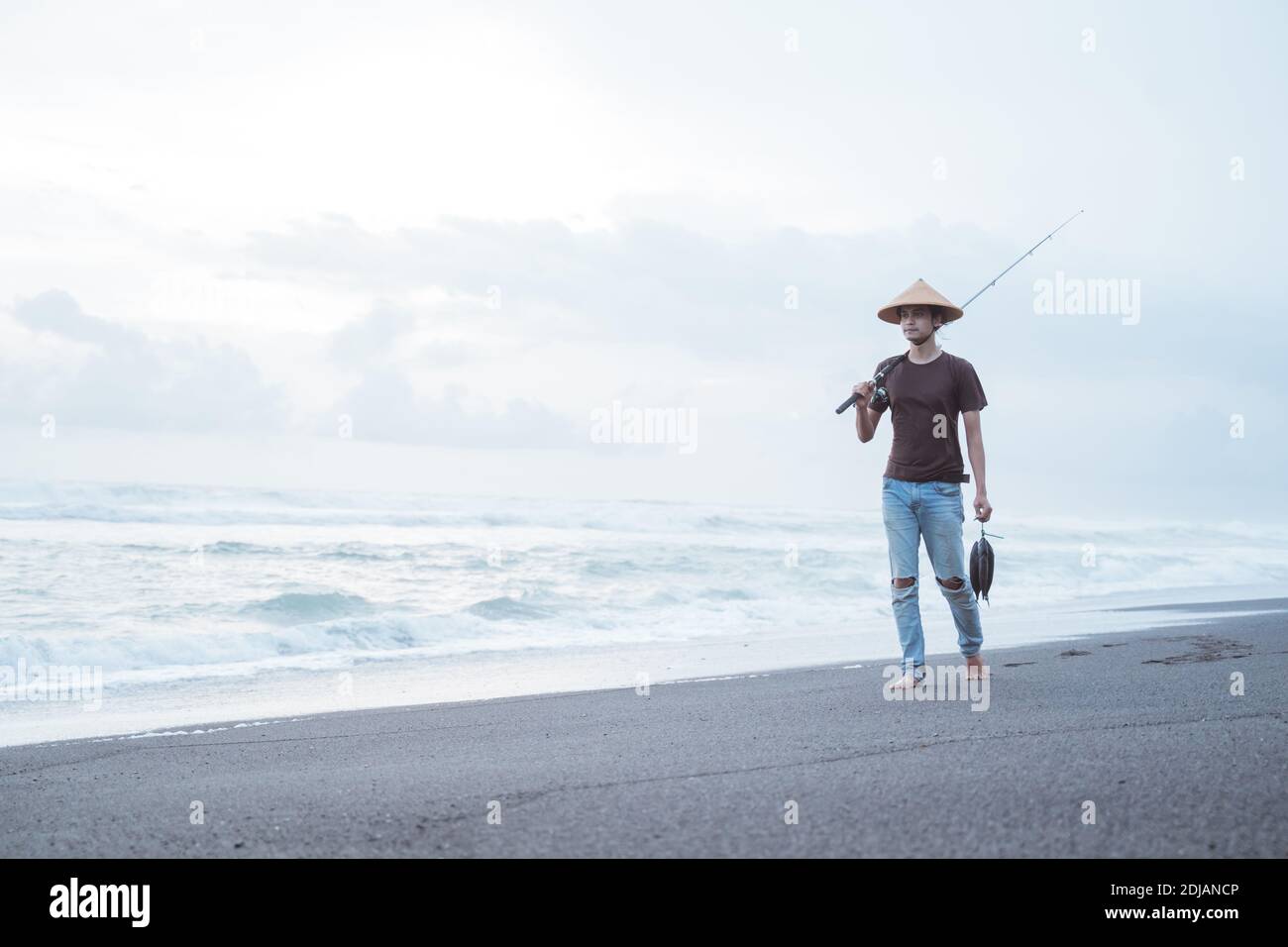 Portrait of a young fisherman walking alone holding captured fish on ...