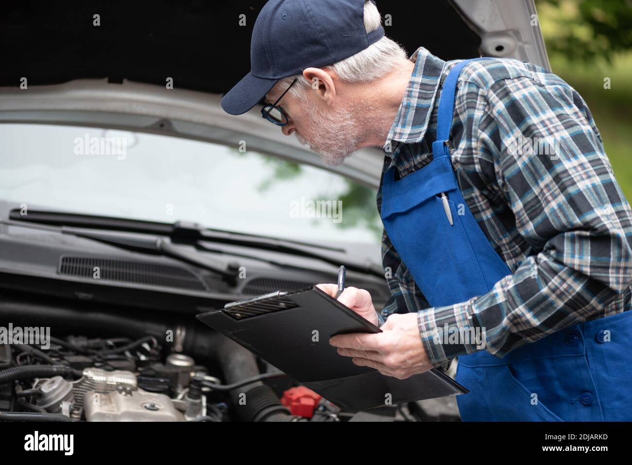 Car mechanic checking a car engine and writing on clipboard Stock Photo ...