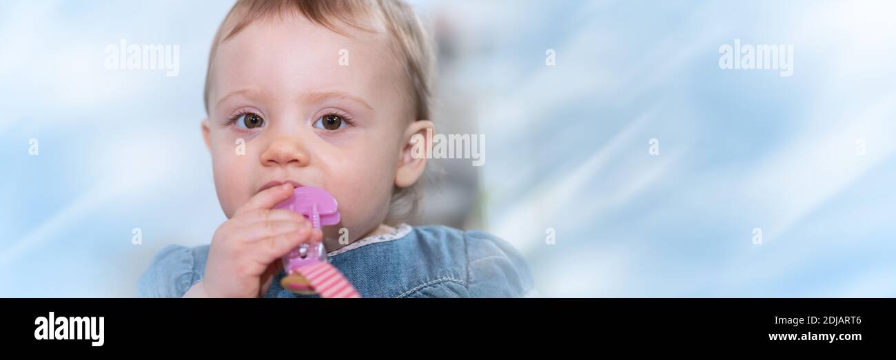 Cute baby girl biting a plastic clip and looking at the camera ...