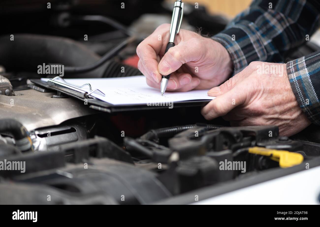 Car mechanic checking a car engine and writing on clipboard Stock Photo ...