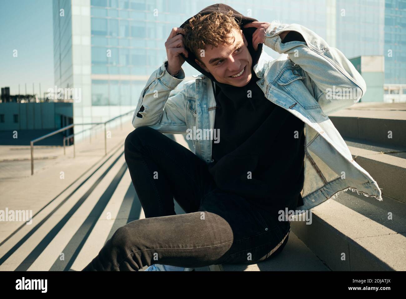 Attractive smiling guy wearing denim jacket and hoodie joyfully resting ...