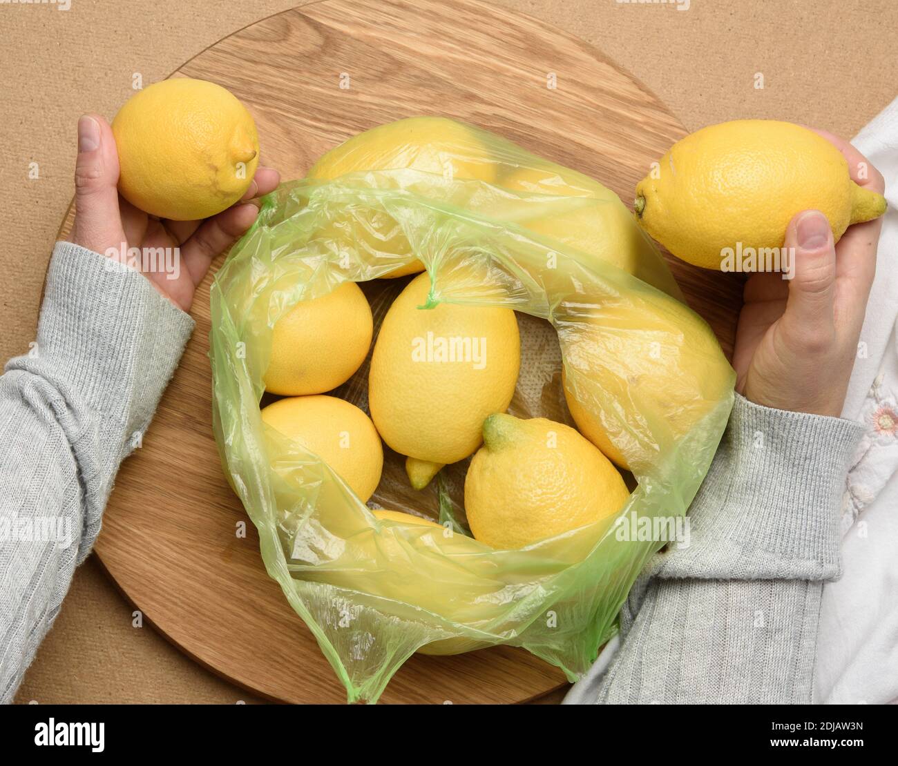 fresh yellow lemons in a plastic bag on a wooden round board, top view ...