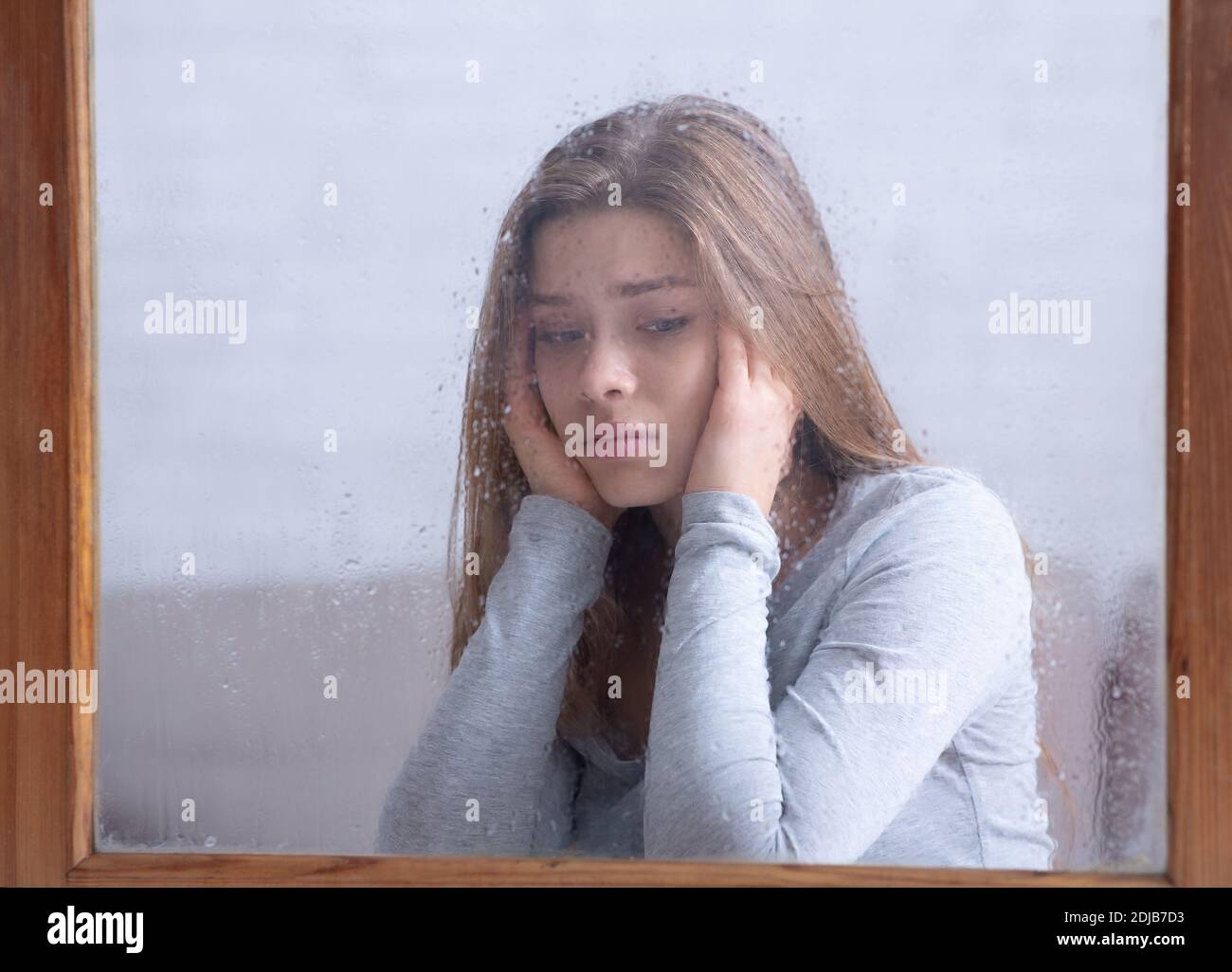 Attractive young lady feeling unhappy because of bad weather, looking ...