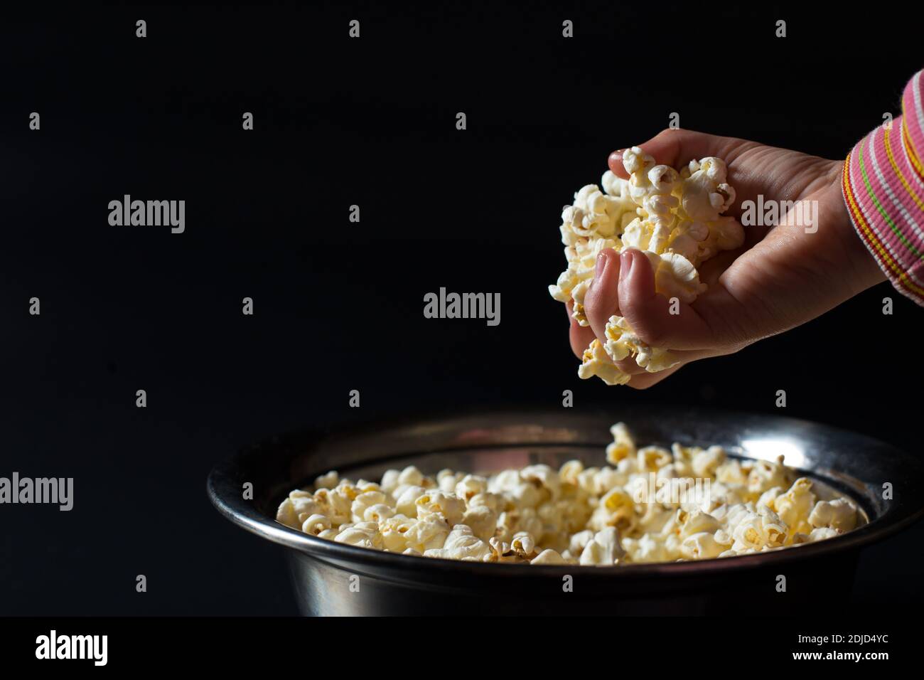 Child's hand taking popcorn from bucket on black background, with ...