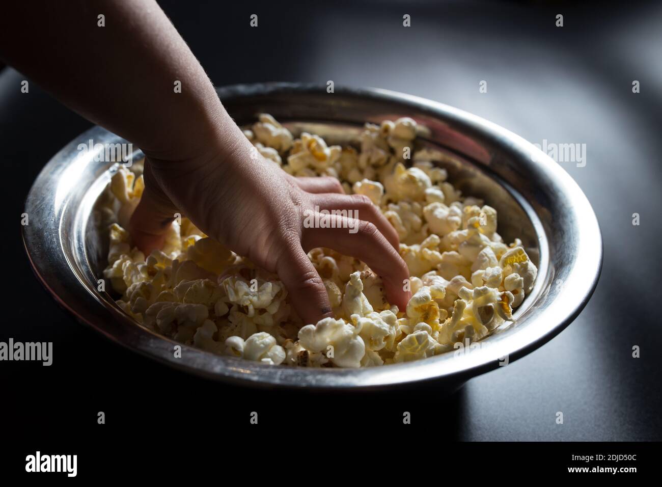 Child hand takes popcorn from bucket against monitor, on black ...