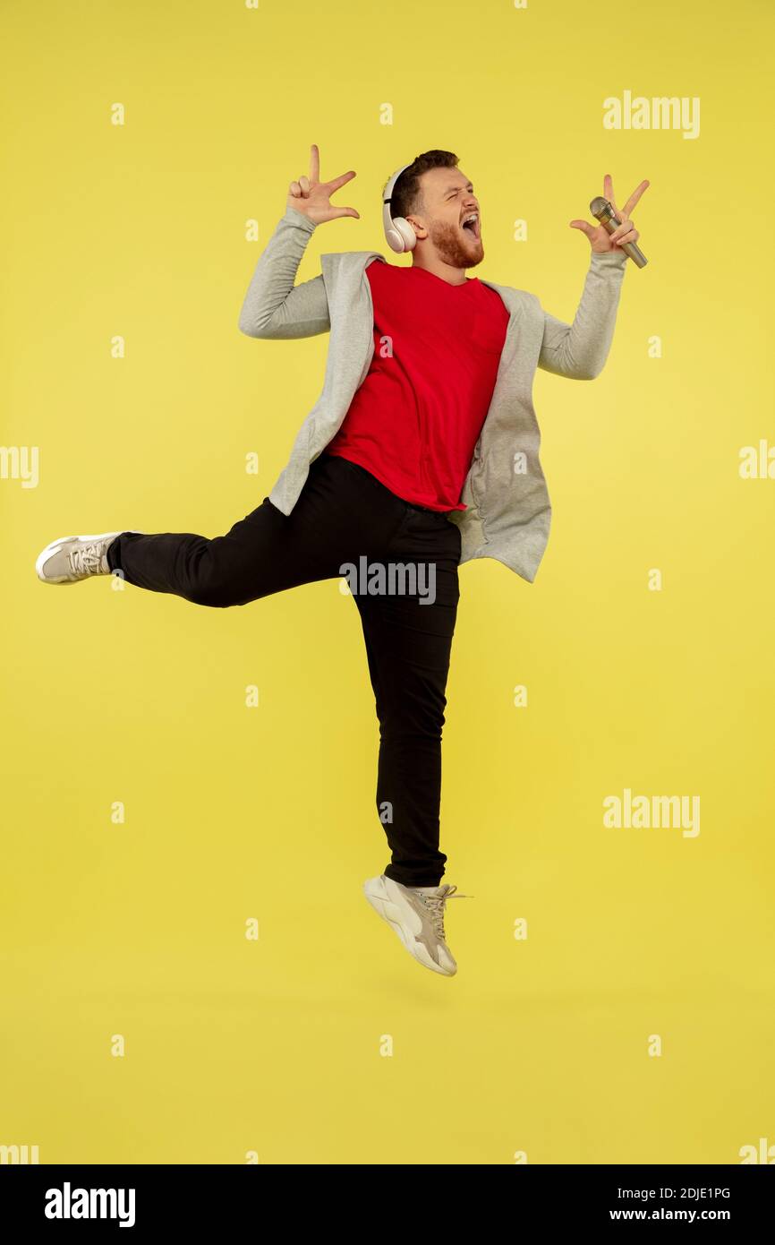 Singing with headphones. Full length portrait of young high jumping man ...