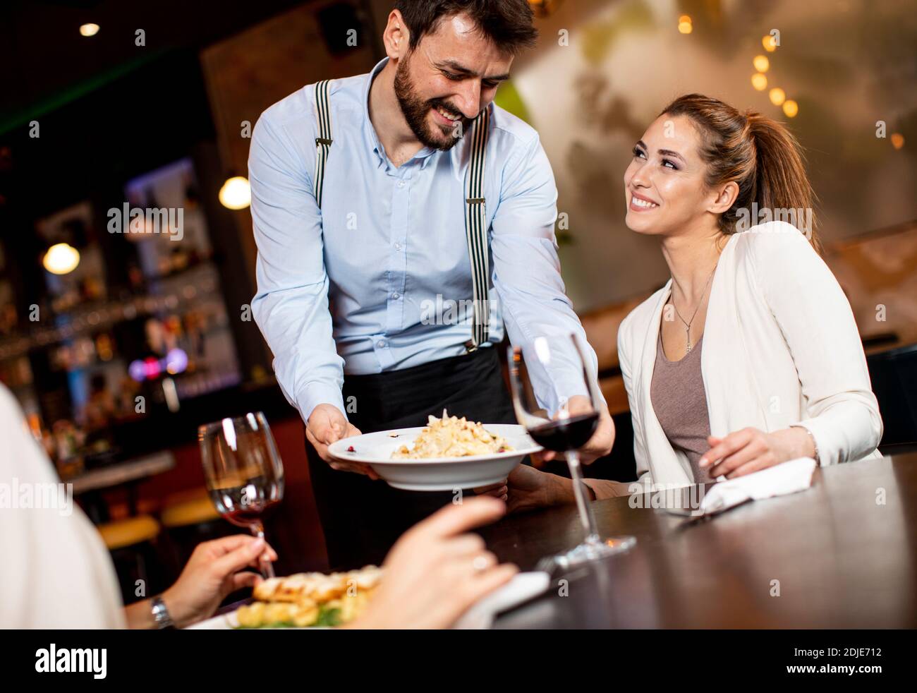 Handsome young waiter serving food to female customers in the ...