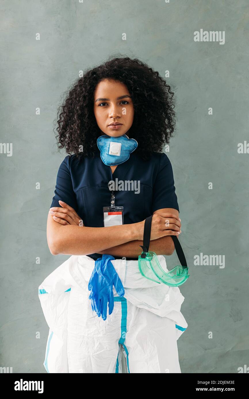 Young serious nurse standing at wall with arms crossed wearing and ...