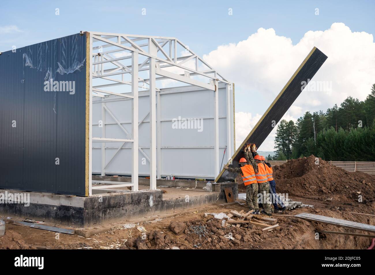 Workers manually install a wall panel on the frame of an industrial ...