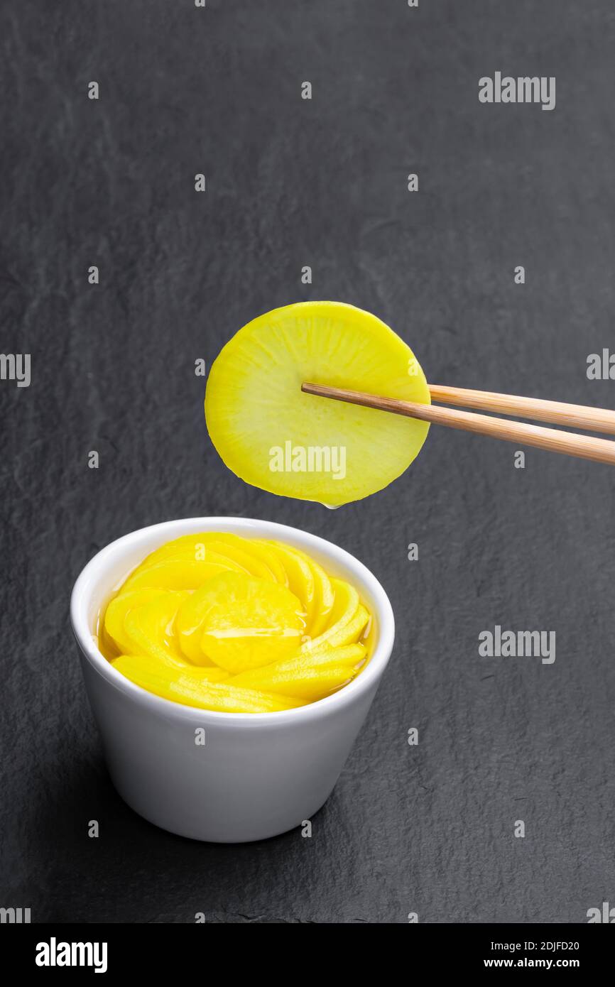 Marinated daikon slice picked up with chopsticks on black stone ...