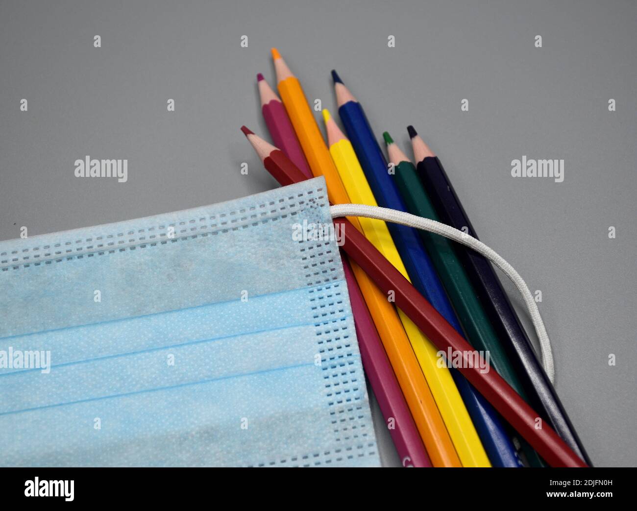 Handful of colored pencils inside the elastic rubber of a surgical mask ...