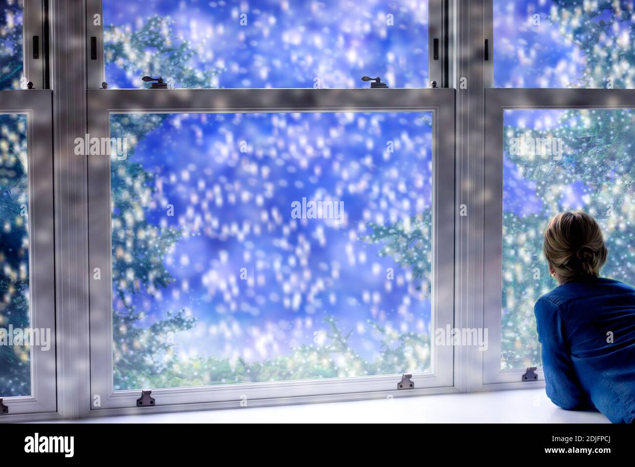 Christmas background. Woman is looking by the window at falling snow ...