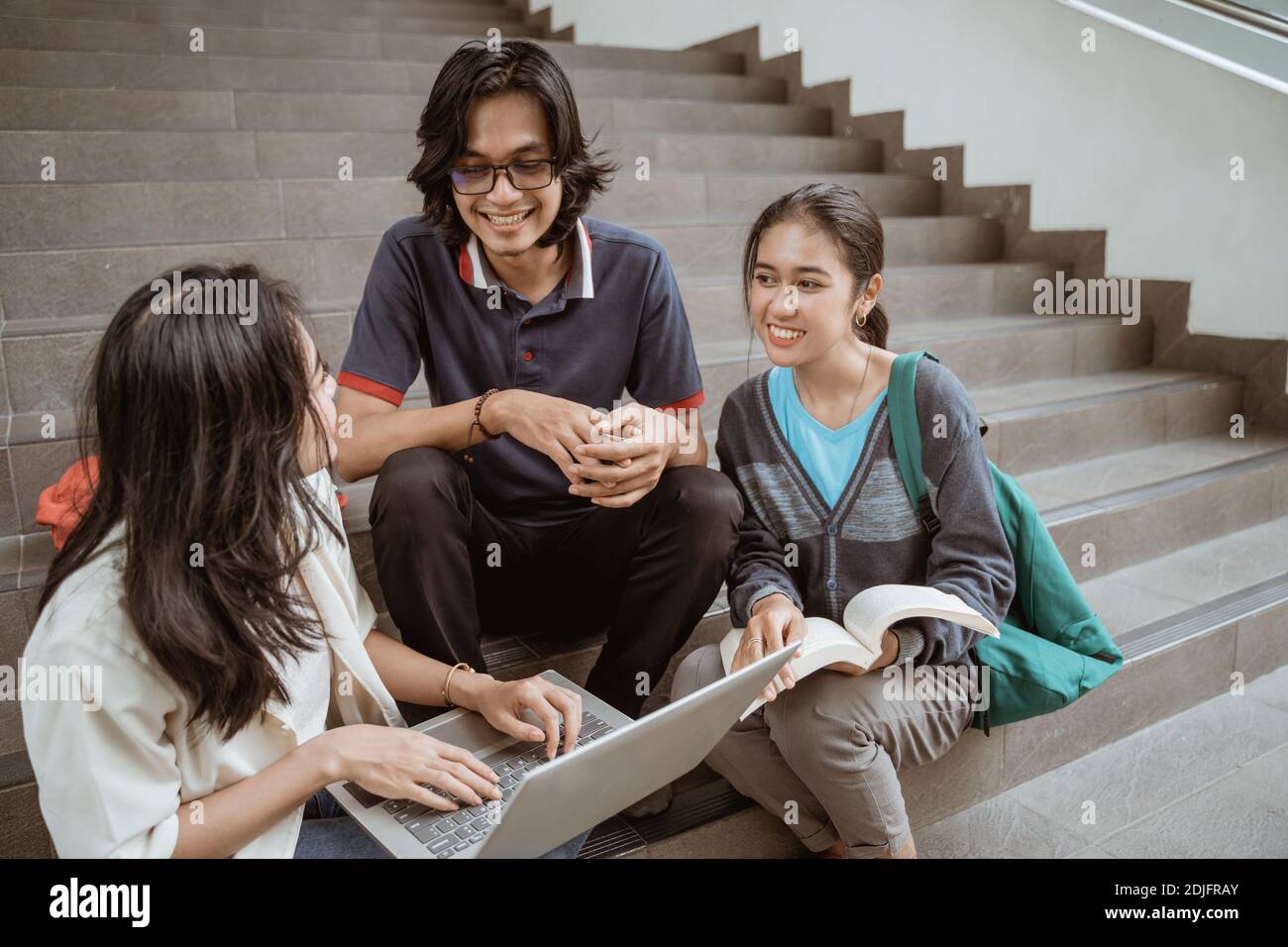 Portrait students sit down working in groups on the floor stairs campus ...