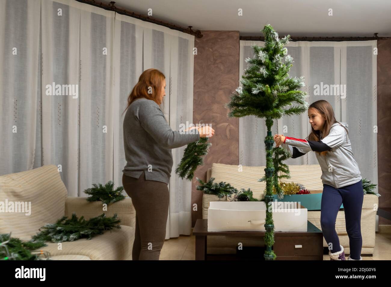 Mother and daughter assembling the Christmas tree in their living room ...