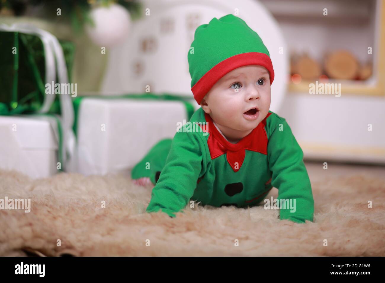 baby boy in red green elf costume sitting under Christmas tree and gift ...