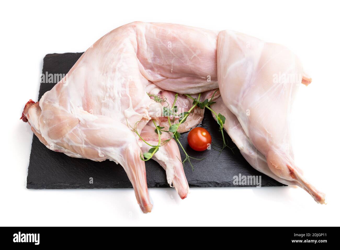 Whole raw rabbit with tomatoes, pea sprouts on a black concrete slate ...