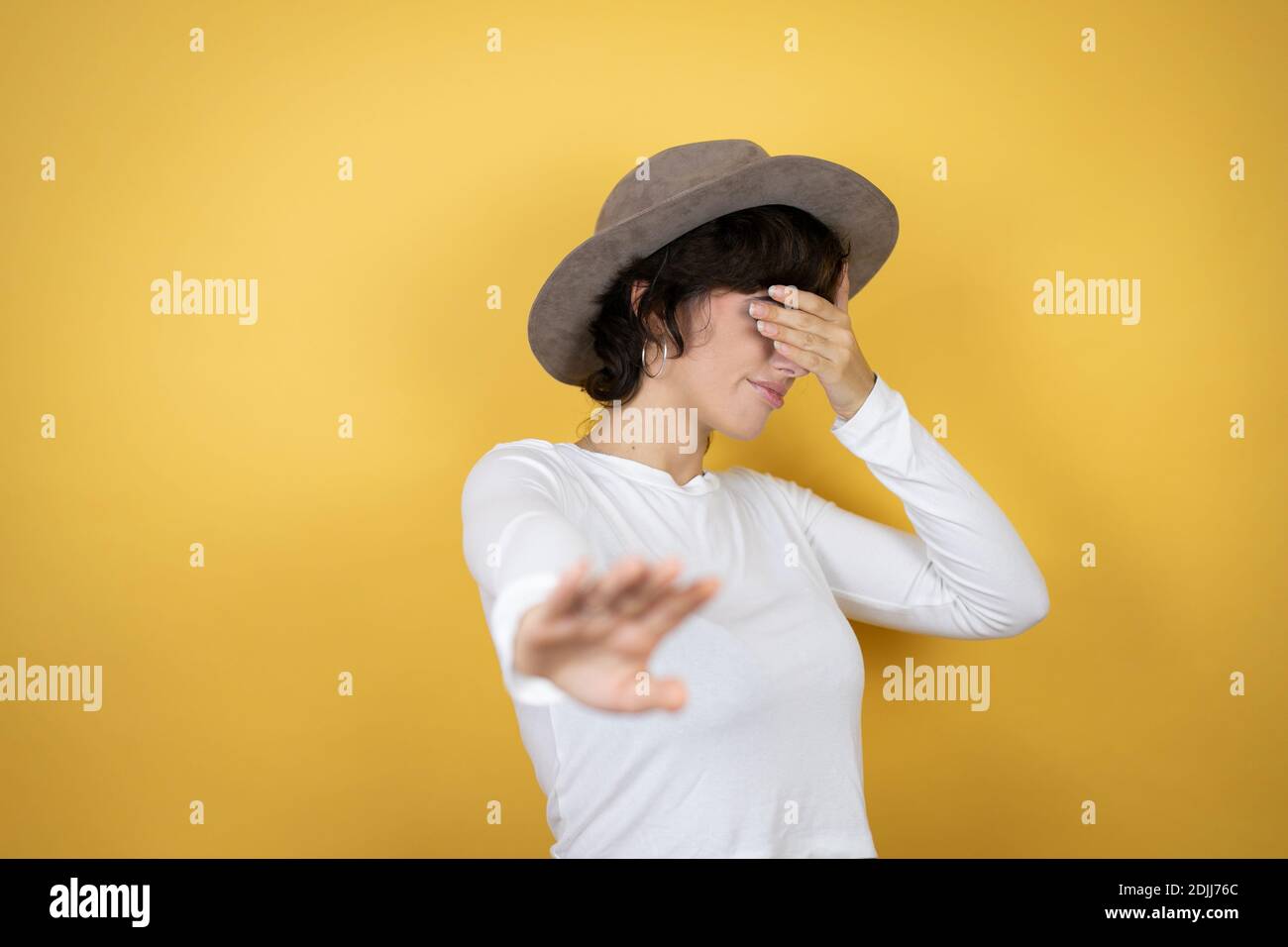 Young caucasian woman wearing hat over isolated yellow background ...