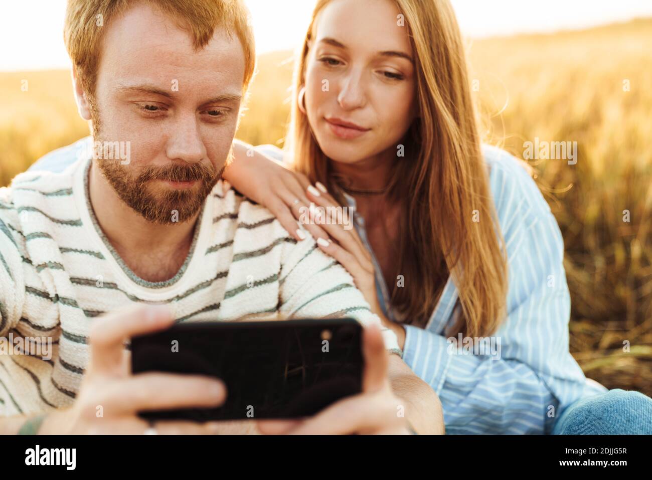 Image of a young loving couple using mobile phone outside at the field ...