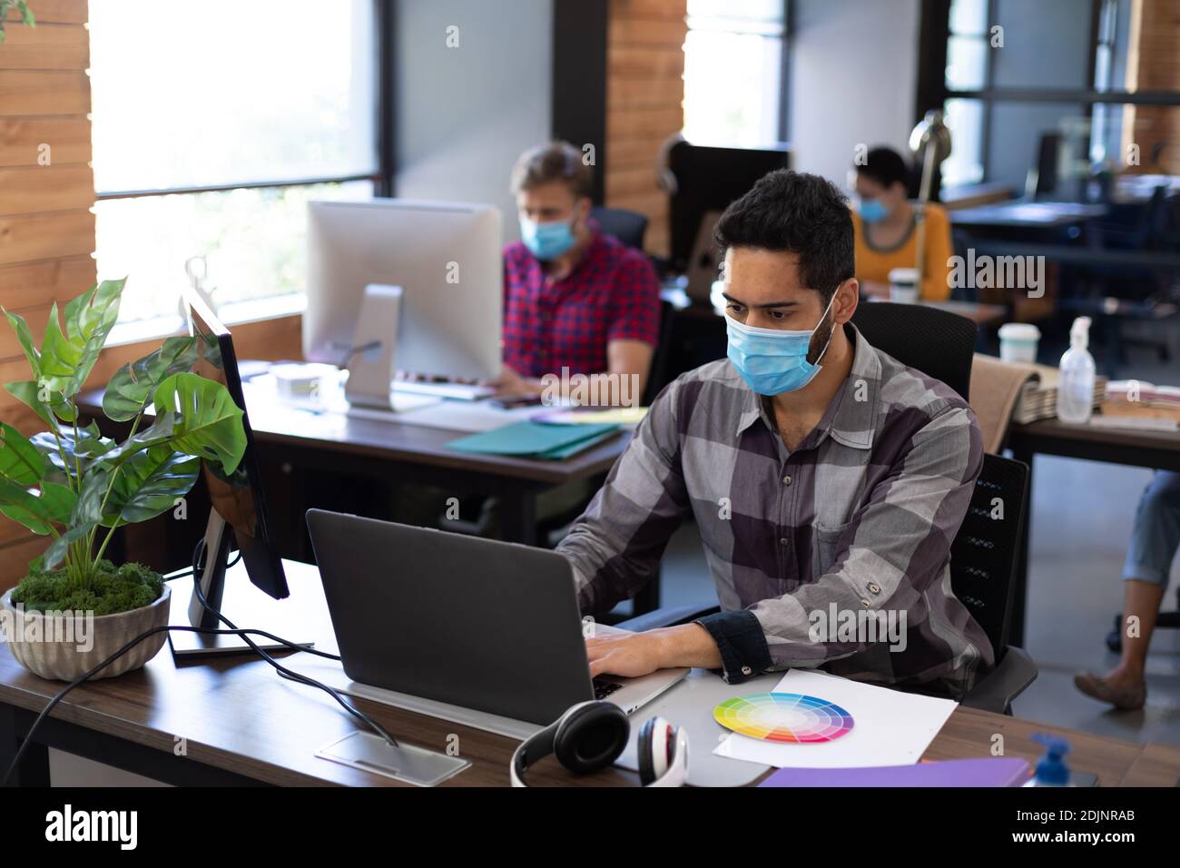 Diverse male colleagues wearing face masks working in computers at ...