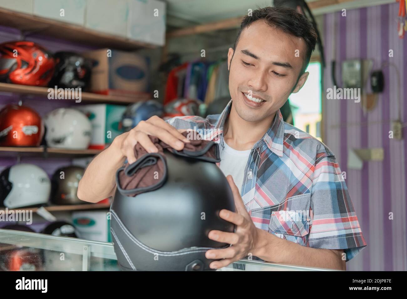 male shop assistant stands cleaning a helmet with a cloth with helmet ...