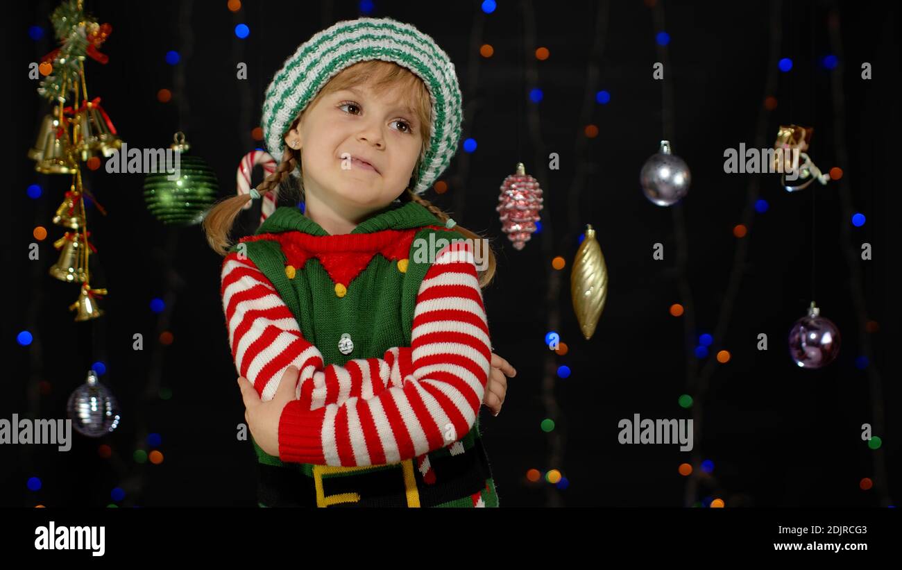 Displesed, tired kid girl in elf Santa helper costume has spoiled mood ...