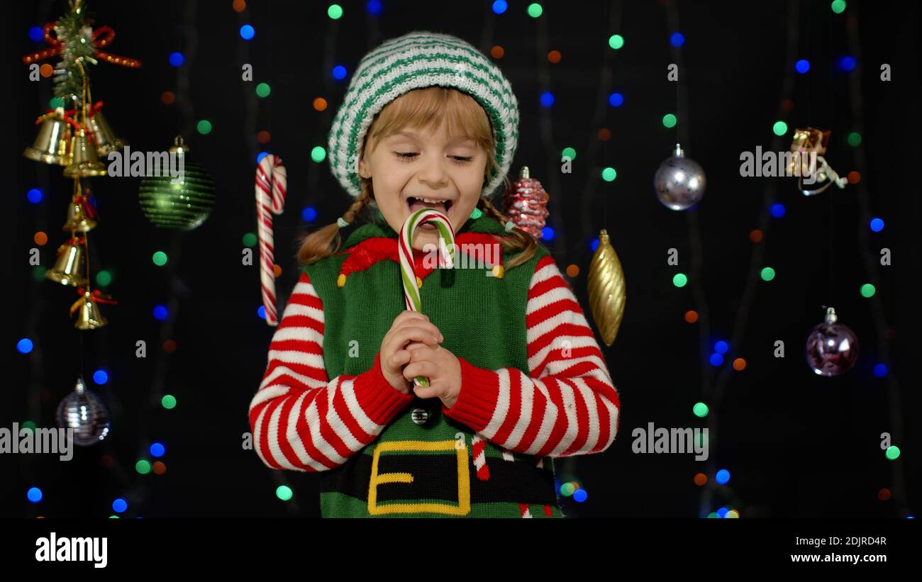 Blonde kid girl in Christmas elf Santa Claus helper costume licking ...