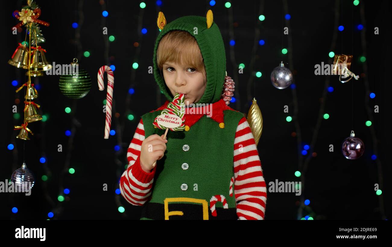 Blonde kid girl in Christmas elf Santa Claus helper costume licking ...