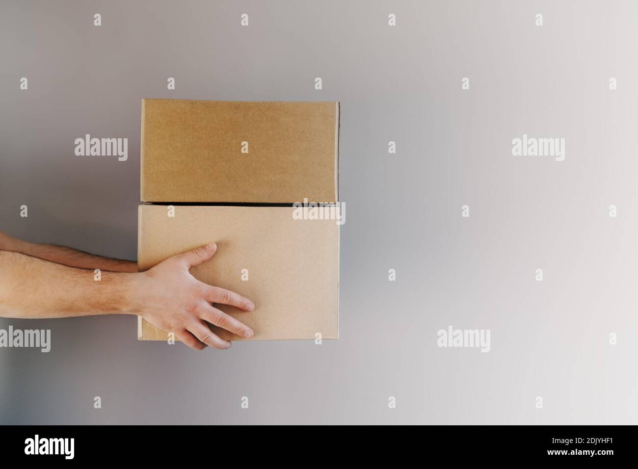 The hands of delivery service man holding carton boxes on the grey ...