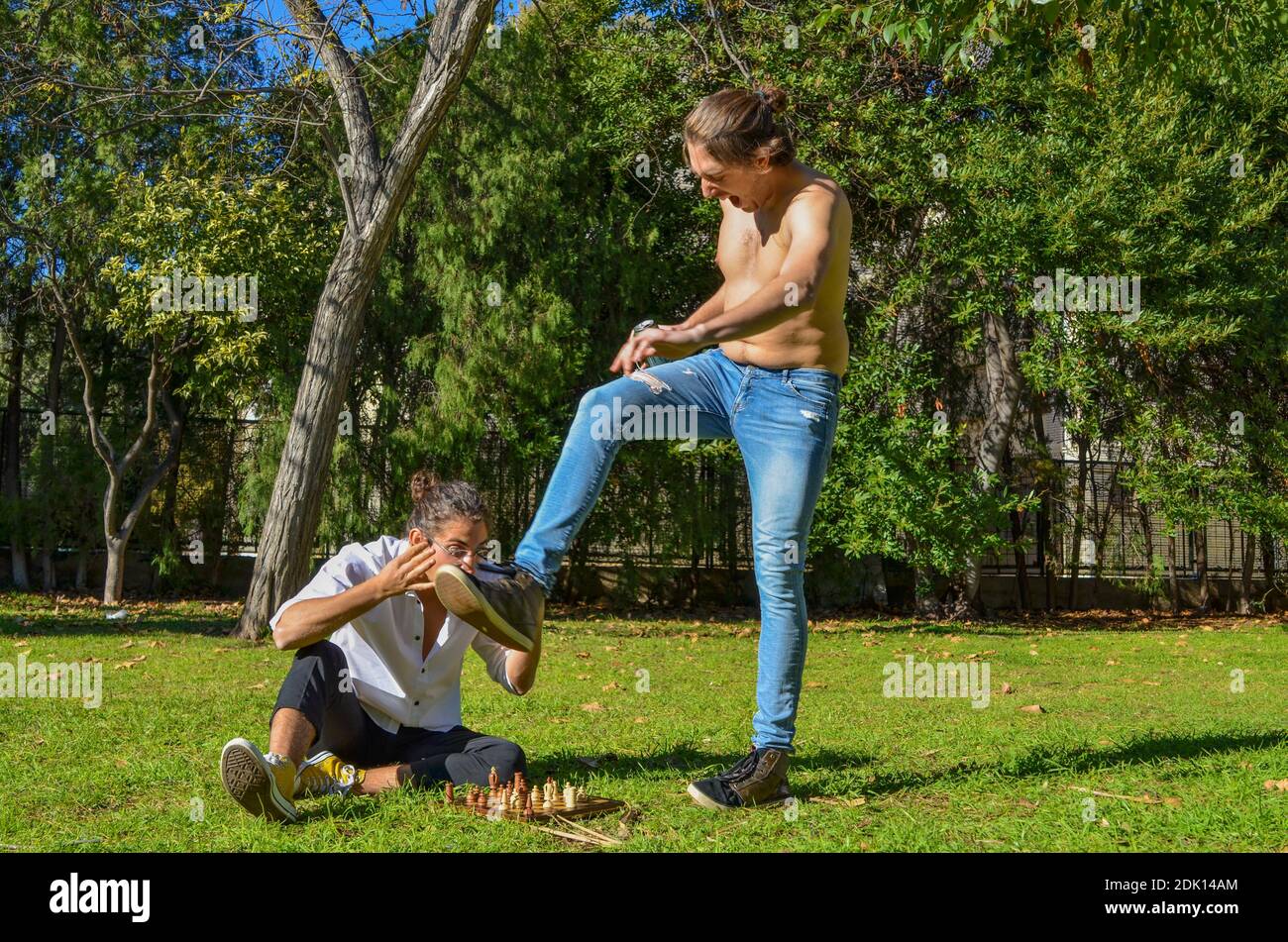 A closeup shot of two men in the garden with chessboard, one man kicks ...