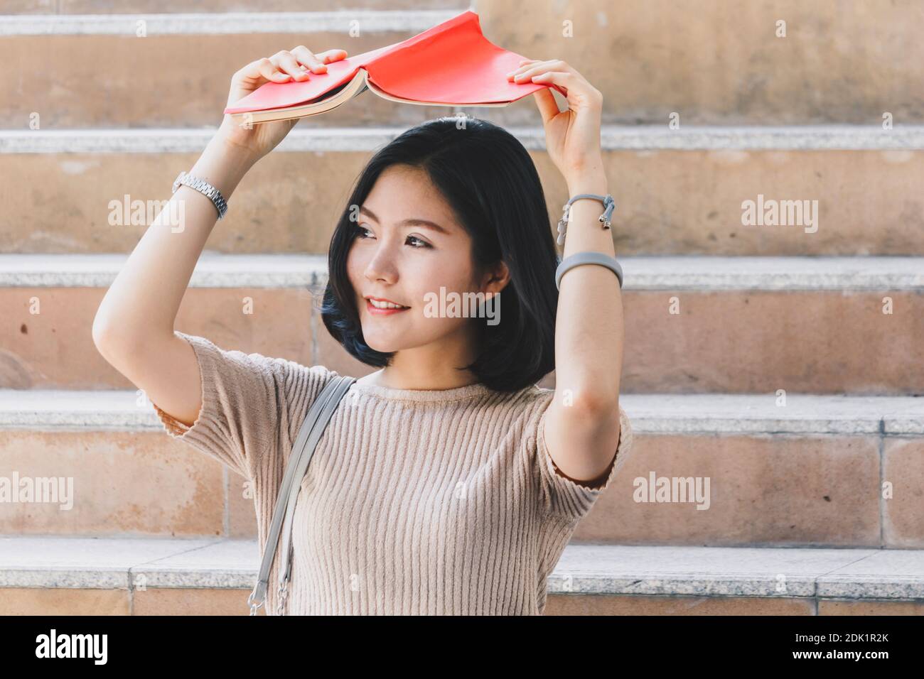 Woman Holding Book Over Head Against Staircase Stock Photo - Alamy