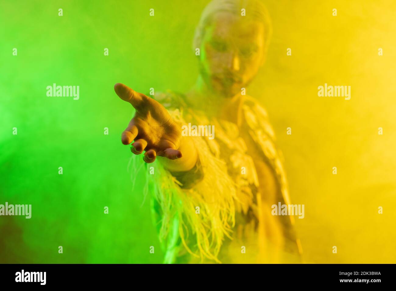 Talented young male dancer reaching hand through green and yellow smoke ...