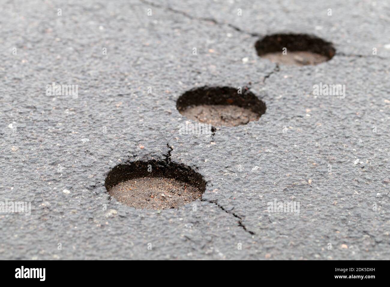 Damaged asphalt road with cracks and pavement test holes, close-up ...