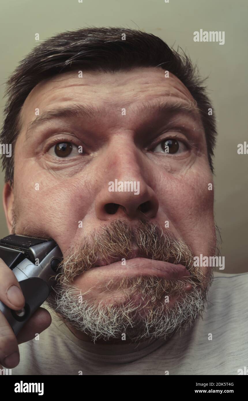 An adult man shaves himself with an electric razor. Unusual portrait of ...