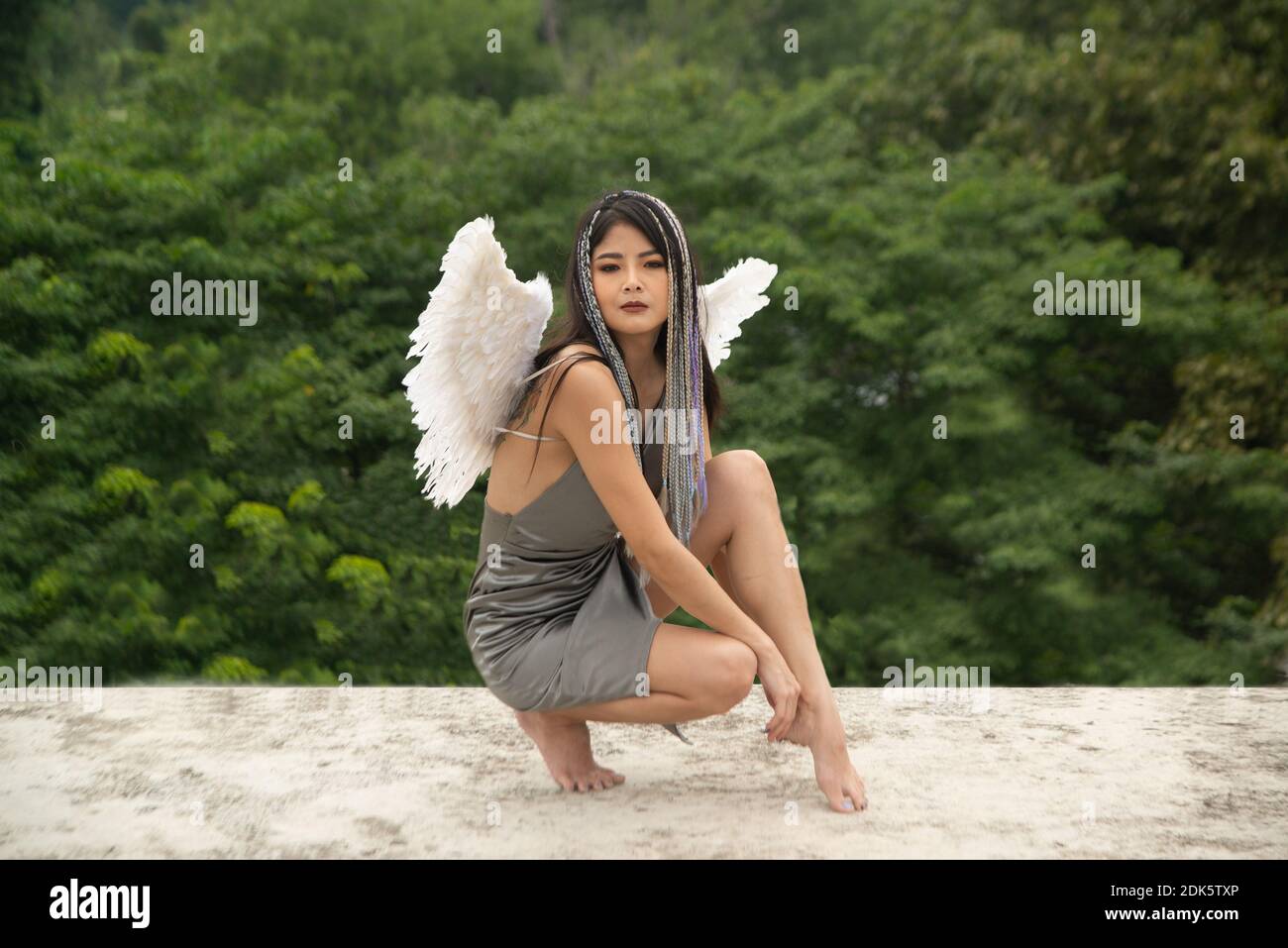 Beautiful Angel Crouching On Land Against Trees Stock Photo - Alamy