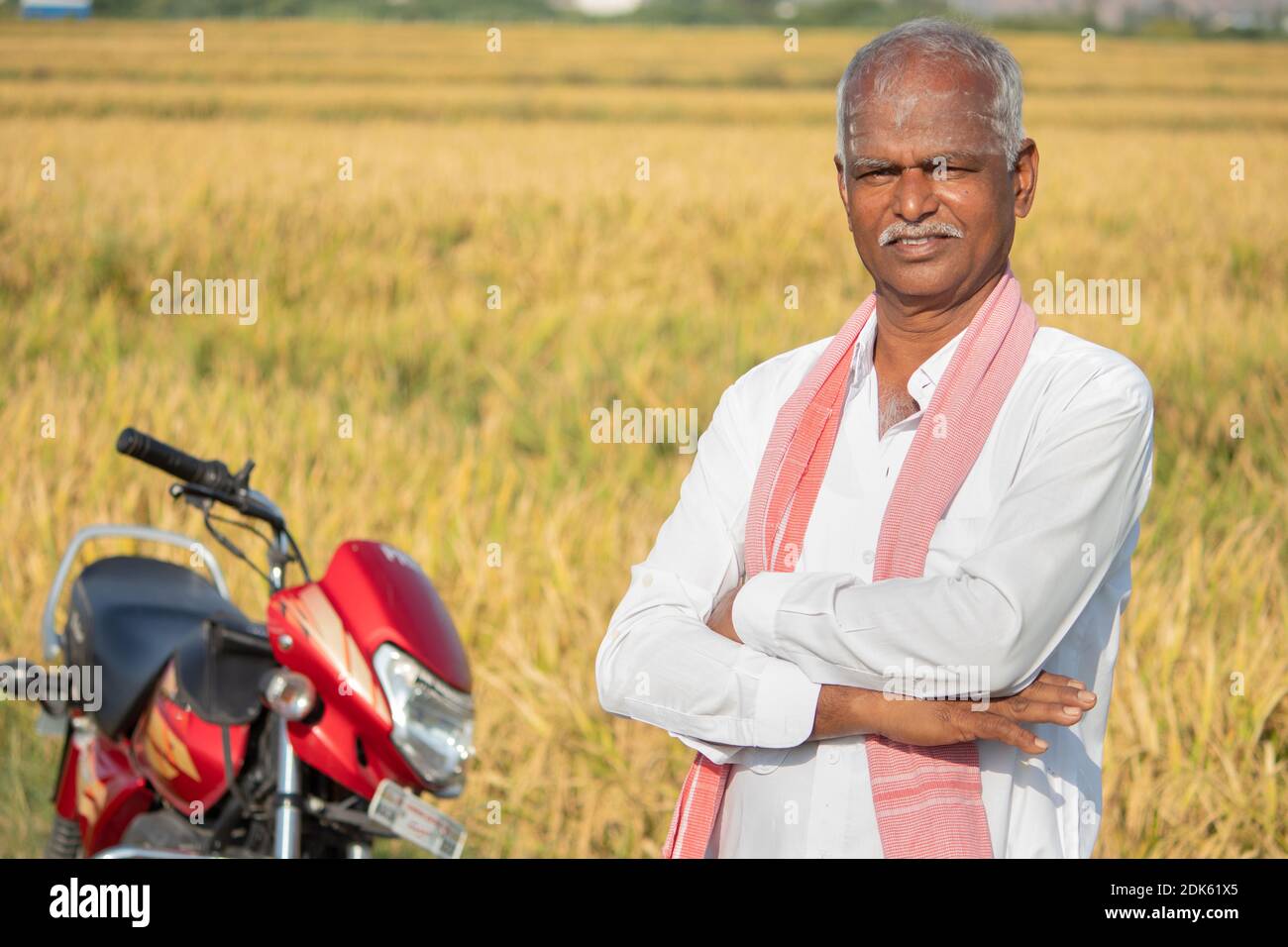 Happy Indian farmer with arms crossed standing with bike infront of the ...