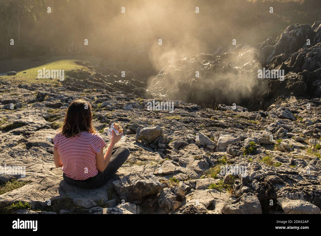 A high angle shot of a young woman biting a sandwich while sitting over ...