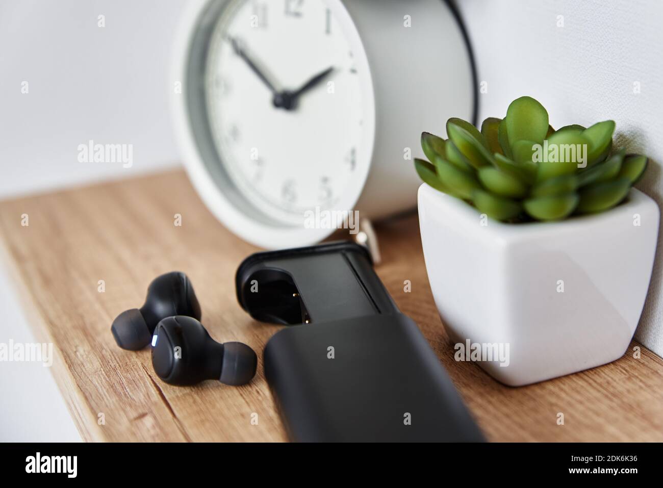 Wireless earphones on the shelf with alarm clock and house plant ...