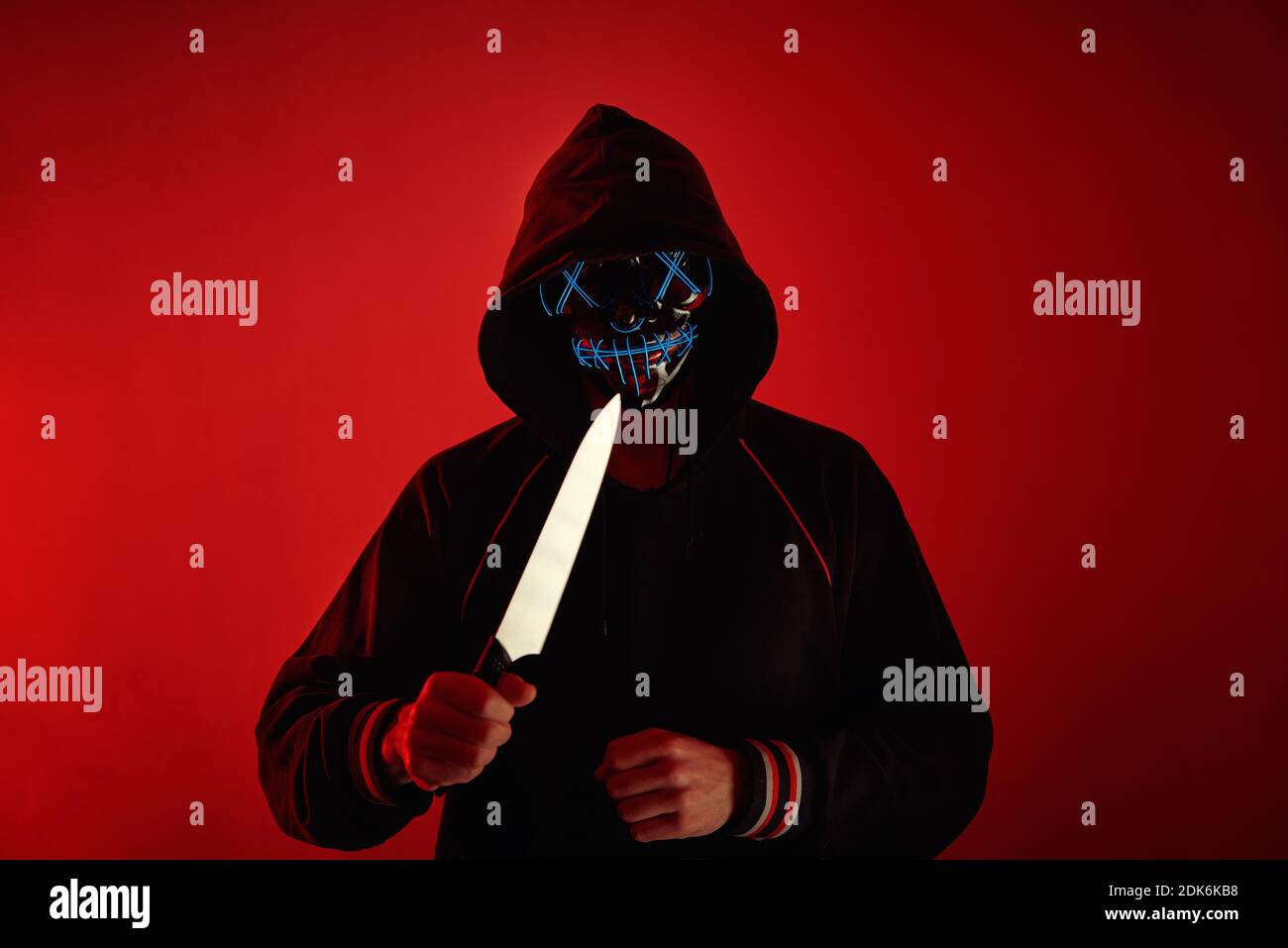 Man in hoodie with scary mask on face holds knife in hand on red ...