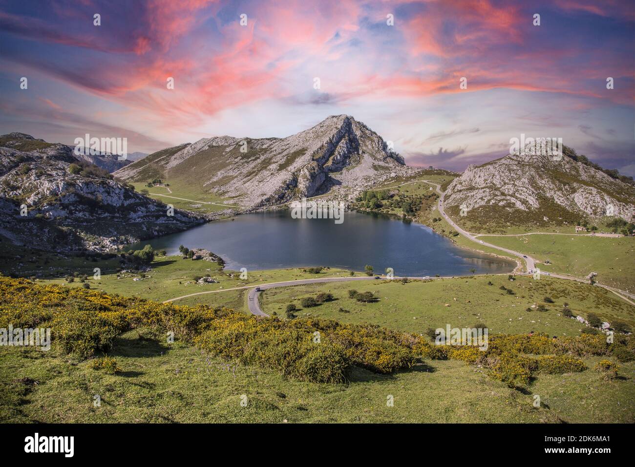 A mesmerizing view of the Lake Enol gleaming under the pink cloudy sky ...