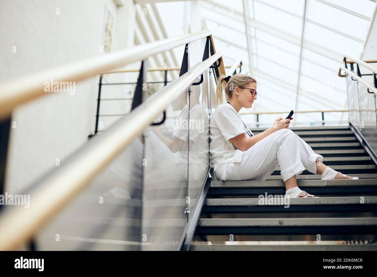Female sitting on stairs while using cell phone Stock Photo - Alamy