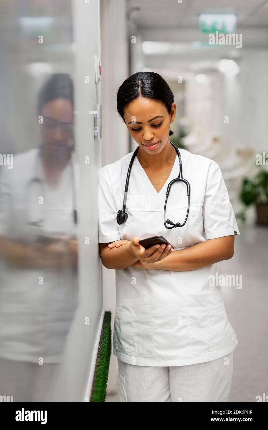 Female doctor using cell phone at corridor Stock Photo - Alamy
