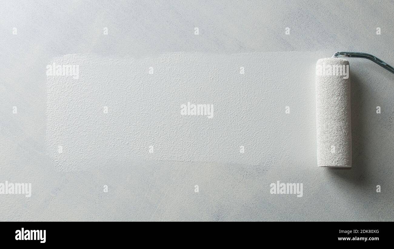Painter's roller draws a stripe of white paint on a white wooden ...