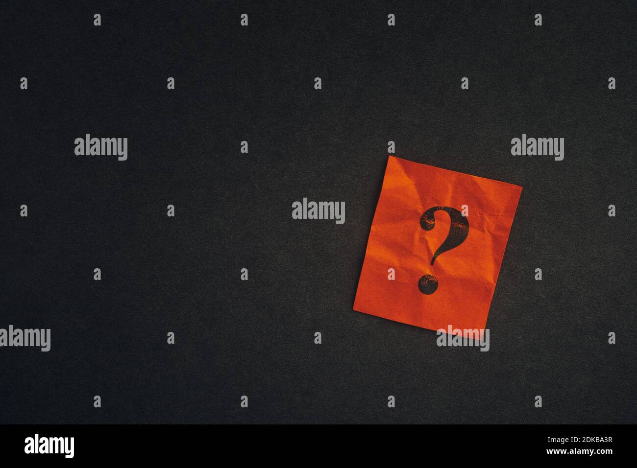 Red paper note with question mark on a black background. Low key. Close ...
