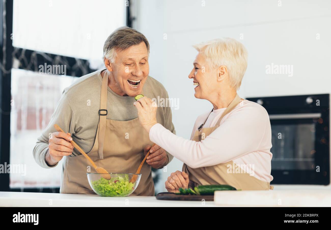 Senior Family Couple Feeding Each Other Cooking Dinner In Kitchen Stock ...