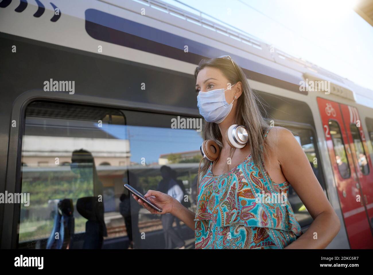 Young woman waiting for train on railway platform, wearing face mask ...