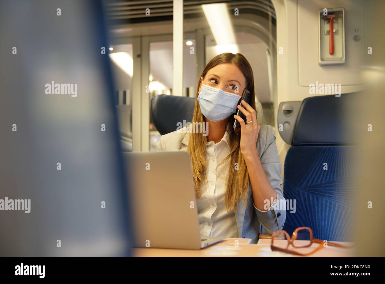 Businesswoman commuting by train, working on laptop and wearing face ...