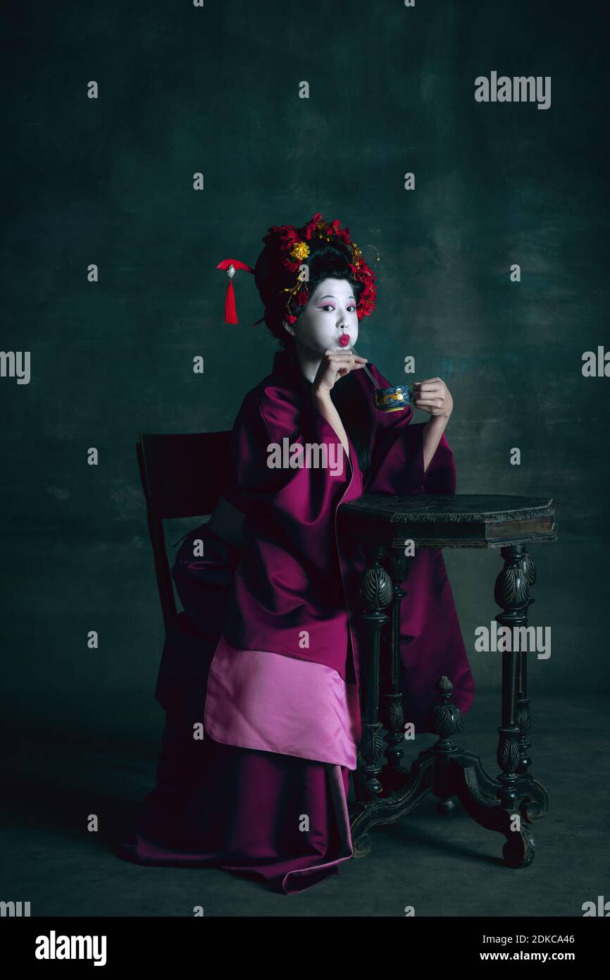 Having fun. Young japanese woman as geisha isolated on dark green ...