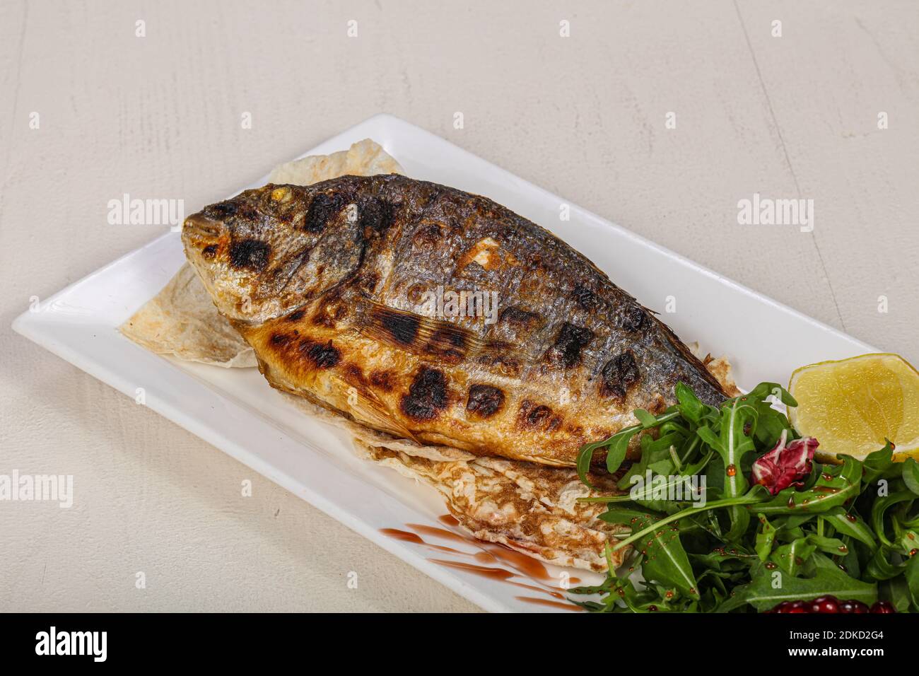 Grilled dorada fish served lemon and rucola Stock Photo - Alamy