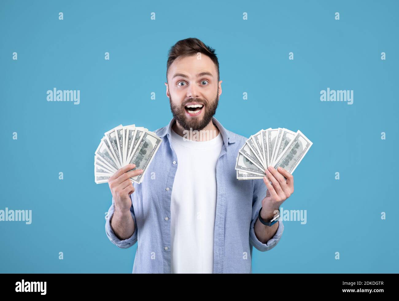 Excited millennial guy holding fan of money banknotes over blue studio ...